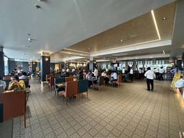 Um restaurante amplo com pé direito alto, iluminação moderna e chão de azulejos.