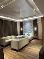 Um quarto moderno com um sofá seccional, uma cama com cabeceira geométrica e piso de madeira.
