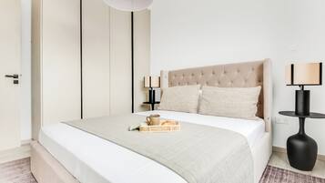 Quarto moderno com uma cama grande, duas mesinhas de cabeceira, uma luminária na parede e uma porta.