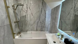 Uma casa de banho moderna com parede de mármore, banheira, toucador com lavatório e zona de duche.