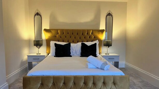 Uma cama grande com cabeceira estofada, duas luminárias de cabeceira e uma toalha dobrada sobre a cama.