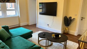 Uma sala de estar com um sofá verde, duas mesinhas de centro redondas e uma TV de tela plana fixada na parede.