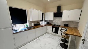 Uma cozinha compacta com armários brancos, piso de mármore, bancada de madeira e coifa preta.