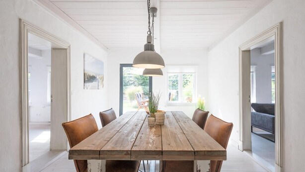 Uma sala de jantar com uma mesa de madeira, seis cadeiras e uma luminária pendente.