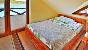 Quarto com cama de madeira, vista para um lago através de uma porta de correr e uma pequena janela.