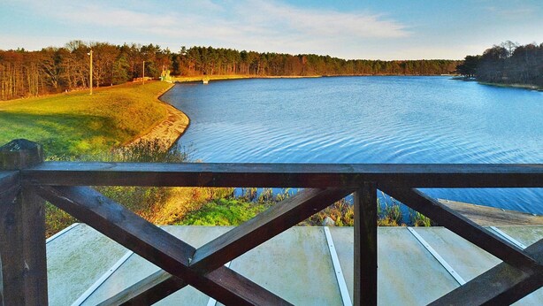 Vista de um deck coberto com vista para um lago tranquilo e margem arborizada.