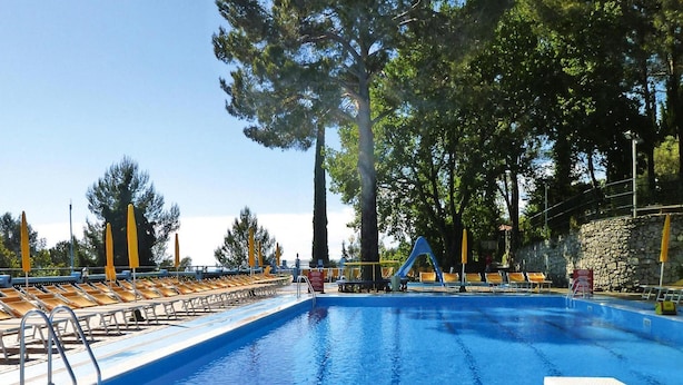 Piscina com escorregador, rodeada por cadeiras de descanso e árvores altas.