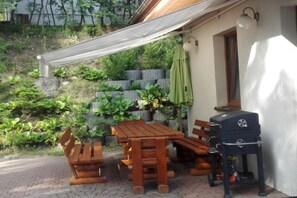 Um pátio com mesa e bancos de madeira, churrasqueira e uma pérgula que oferece sombra.