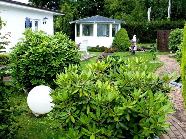 Um jardim com uma casa branca, um gazebo e uma escultura esférica branca.