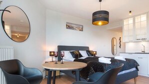 Quarto moderno com cama, mesas de cabeceira, uma mesa redonda, duas cadeiras, um espelho e um lustre.