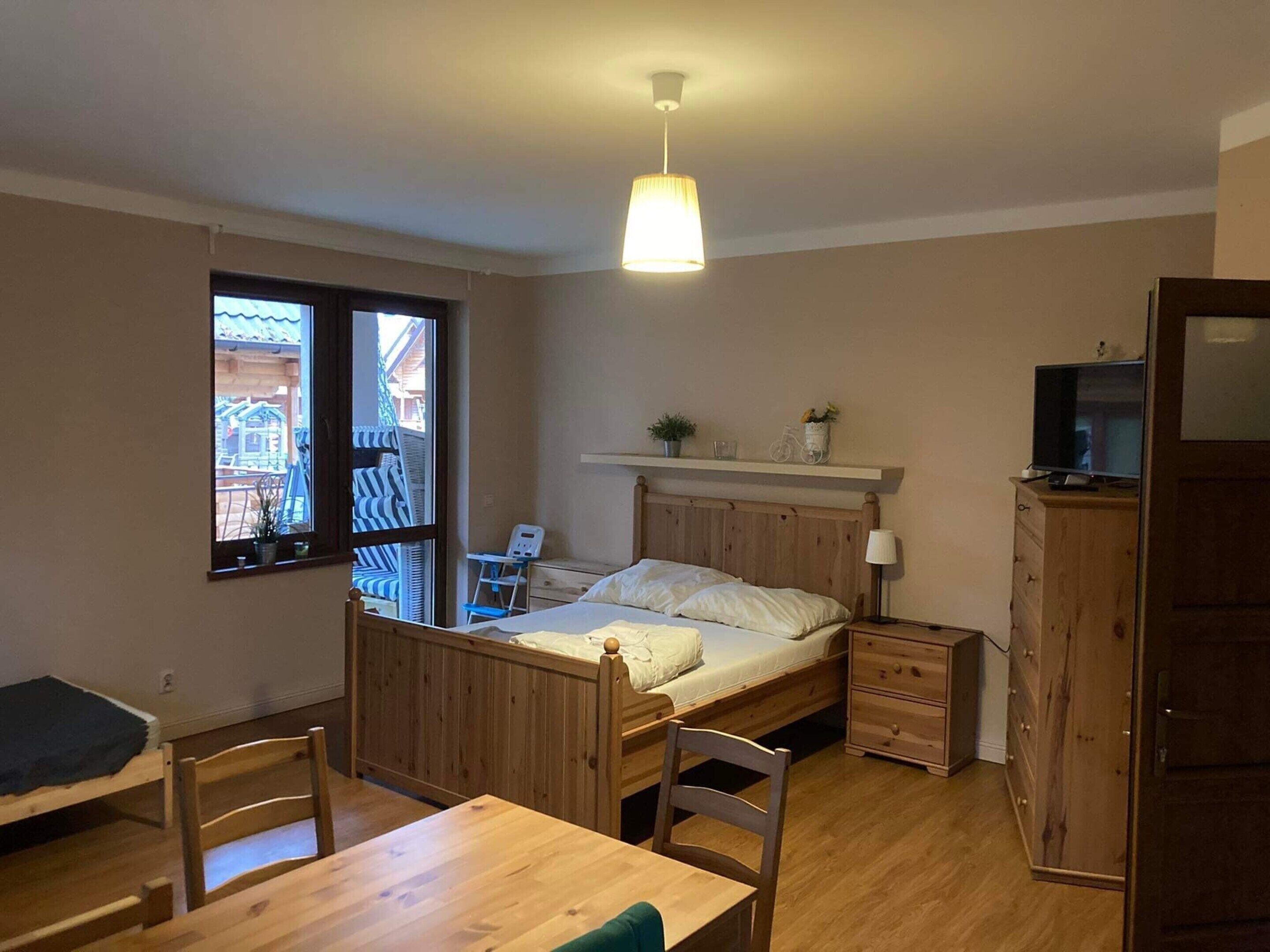 Quarto aconchegante com uma cama, uma mesa de madeira, uma cadeira, uma TV e uma janela com vista para um edifício.