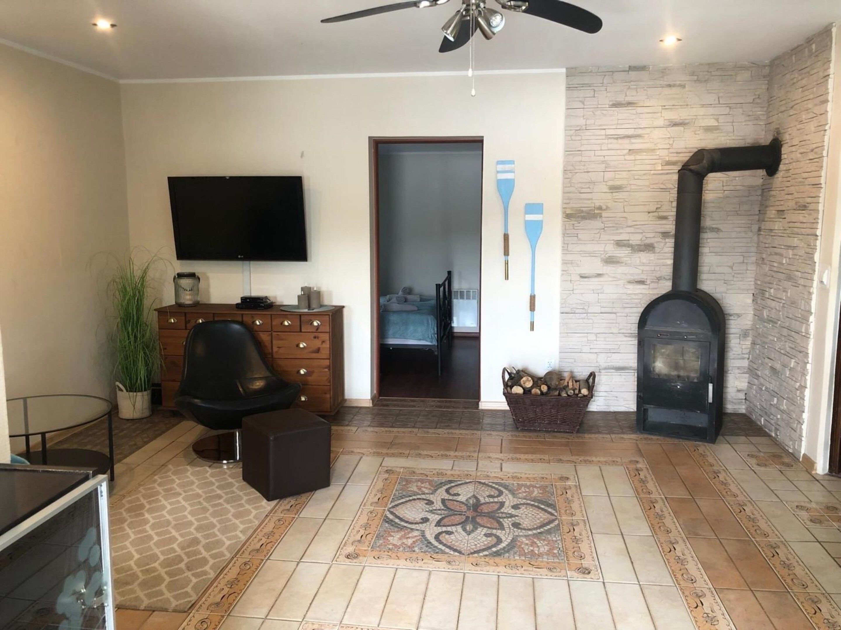 Sala de estar com lareira, televisão, ventoinha no teto e tapete estampado.