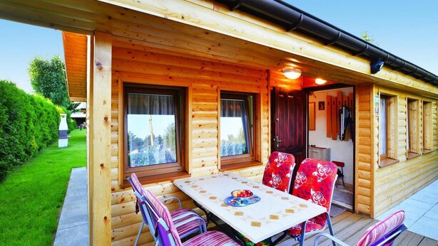 Uma cabana de madeira com mesa e cadeiras, um alpendre coberto e vista para o verde ao redor.