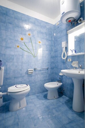 Uma casa de banho com azulejos azuis, sanita, bidé, lavatório e espelho.