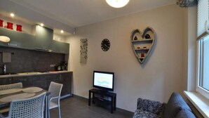 Uma sala de estar moderna com sofá, mesa de jantar com cadeiras, televisão e área de cozinha com armários e um relógio.