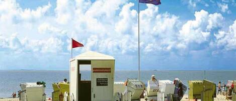 Uma praia com um posto de salva-vidas, uma bandeira e cabanas.