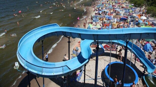 Parque aquático com vários toboáguas e área de praia com guarda-sóis e pessoas.