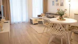 Uma sala de estar moderna com sofá, uma mesa de jantar com cadeiras e uma janela grande com cortinas.