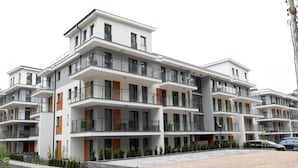 Um edifício residencial de vários andares com varandas, entrada com calçada de brita e carros estacionados.