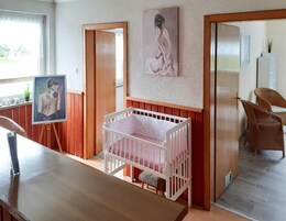 Quarto de bebê com berço, painéis de madeira, um quadro na parede e cadeiras de vime.