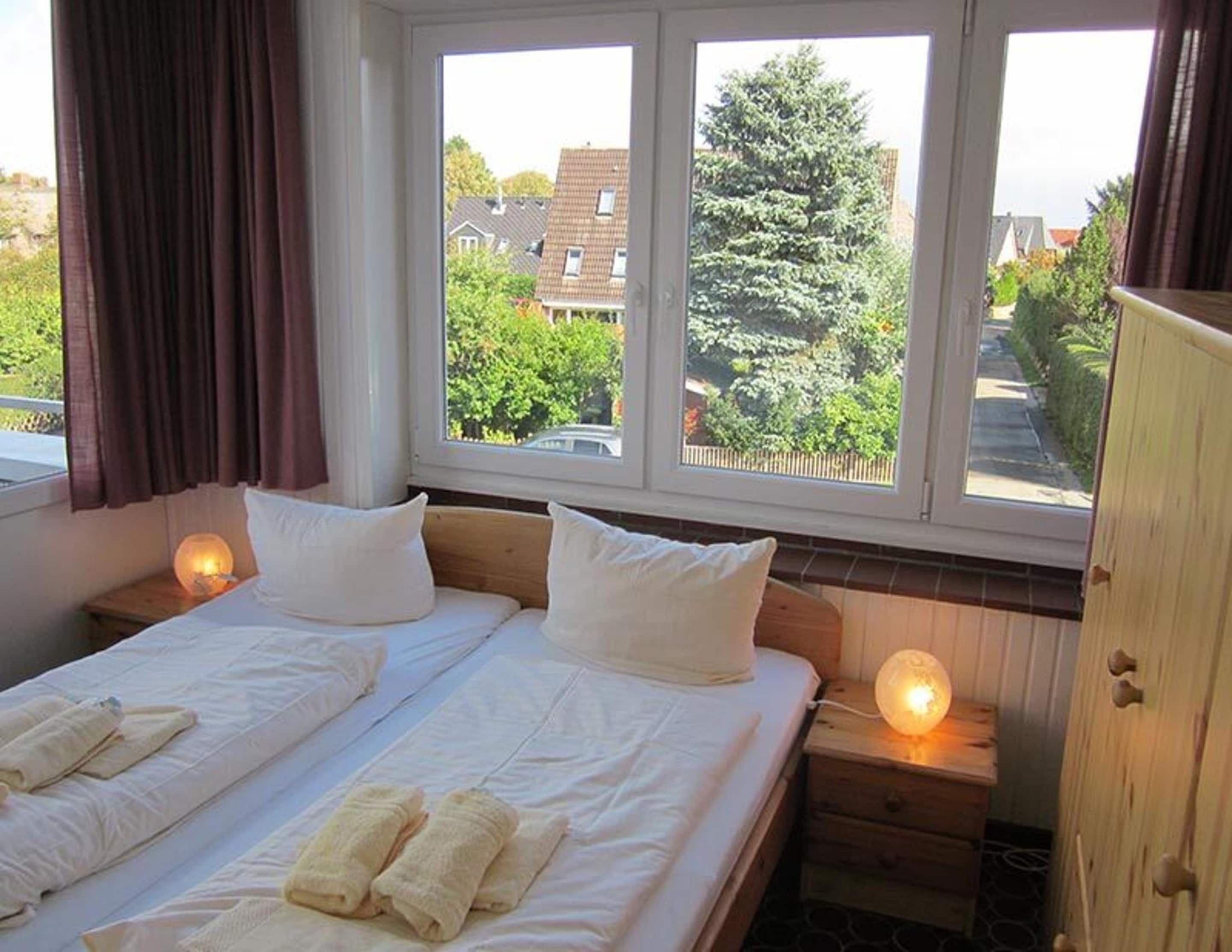 Quarto duplo com duas camas, janela com vista para casas e árvores, e luminárias de cabeceira.