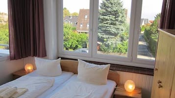 Quarto duplo com duas camas, janela com vista para casas e árvores, e luminárias de cabeceira.