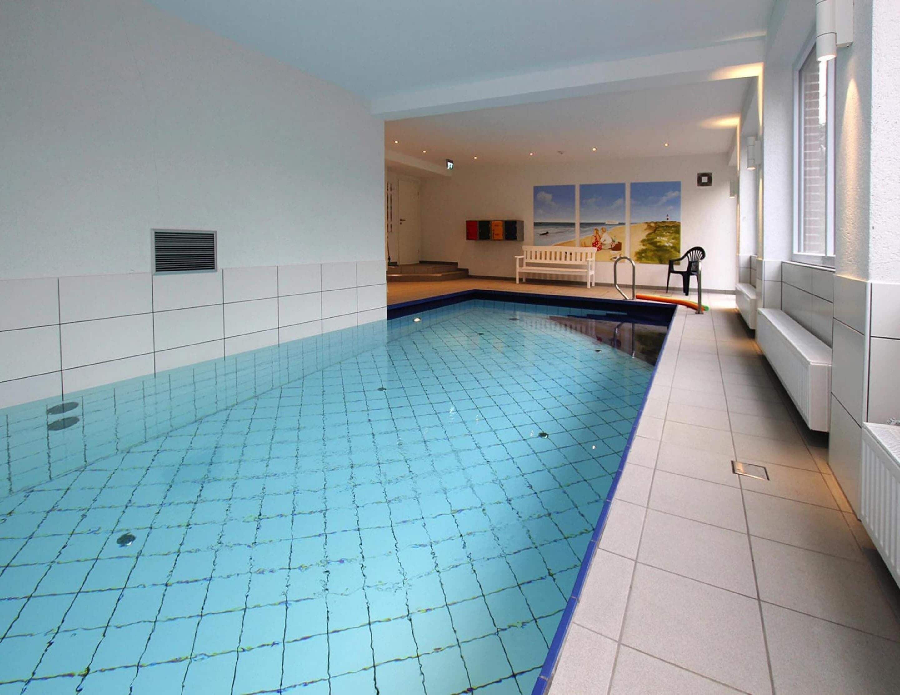 Piscina interior com chão em azulejo, um banco e vista para o mar pelas janelas.