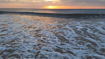 Uma praia com ondas e um pôr do sol ao fundo.