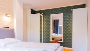 Quarto de hotel com duas camas, piso de madeira, espelho e papel de parede estampado.