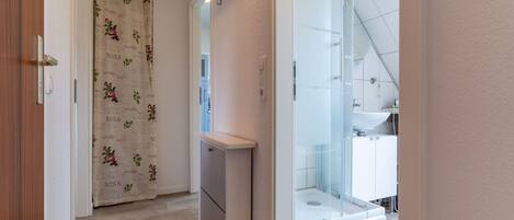 Uma casa de banho moderna com chuveiro em cabine de vidro, lavatório branco e bancada pequena.