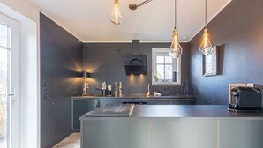 Cozinha moderna com ilha central, iluminação pendente e vista para o exterior.