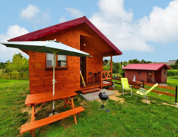 Uma cabana de madeira com varanda, mesa de piquenique e churrasqueira.