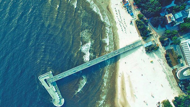 Vista aérea de uma área costeira com uma ponte ligando uma praia a uma península.