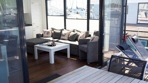 Sala moderna com sofá, mesa de centro e vista para barcos através de amplas janelas.
