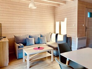 Um quarto aconchegante com piso de madeira, um sofá com almofadas, uma mesa pequena e uma cadeira.