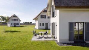 Uma casa moderna com telhado de palha, um pátio com mobiliário externo e um gramado bem cuidado.