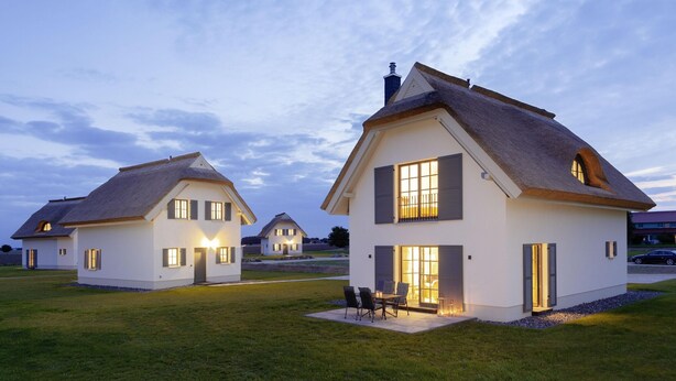 Duas casas modernas com telhados inclinados e janelas amplas, localizadas numa área gramada sob um céu limpo.
