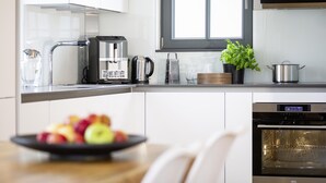 Uma cozinha moderna com armários brancos, uma cafeteira, um bule, uma panela e uma tigela com frutas na bancada.
