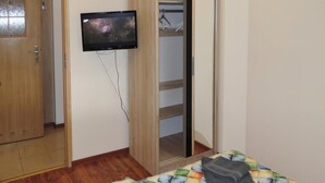 Quarto com cama, televisão na parede, guarda-roupa de madeira e roupeiro com porta deslizante.