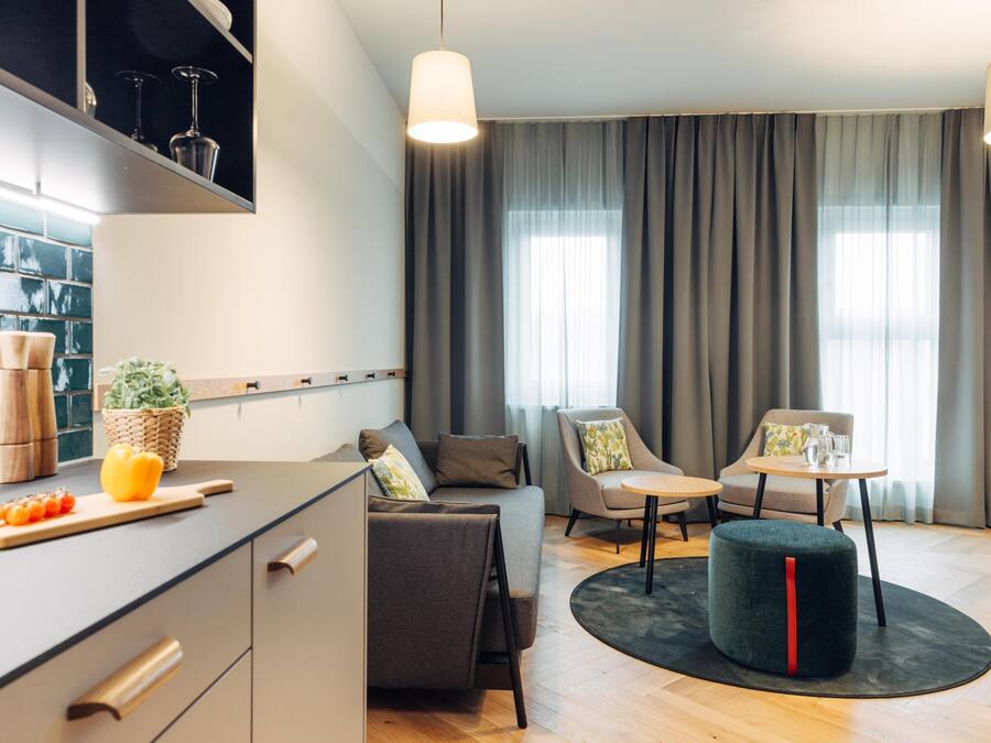 Uma sala de estar moderna com sofá, duas poltronas, uma mesa redonda e uma cozinha com tábua de corte, tomates e uma planta.