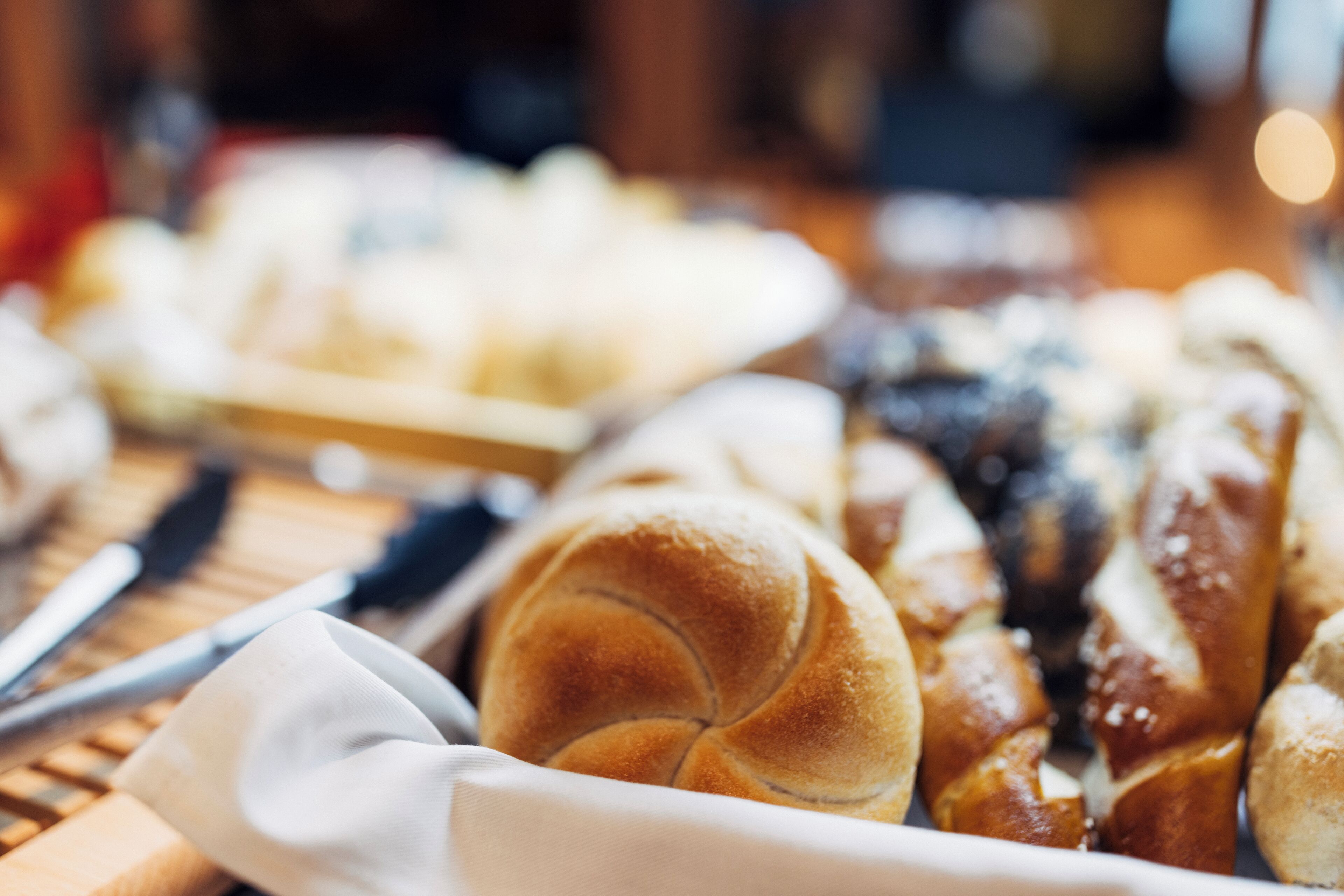 Uma bandeja com pães recém-assados, incluindo um pão trançado e um pão retorcido, sobre uma mesa de madeira.