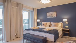 Quarto de hotel com uma cama grande, um banco, uma escrivaninha e vista para a cidade pela janela.