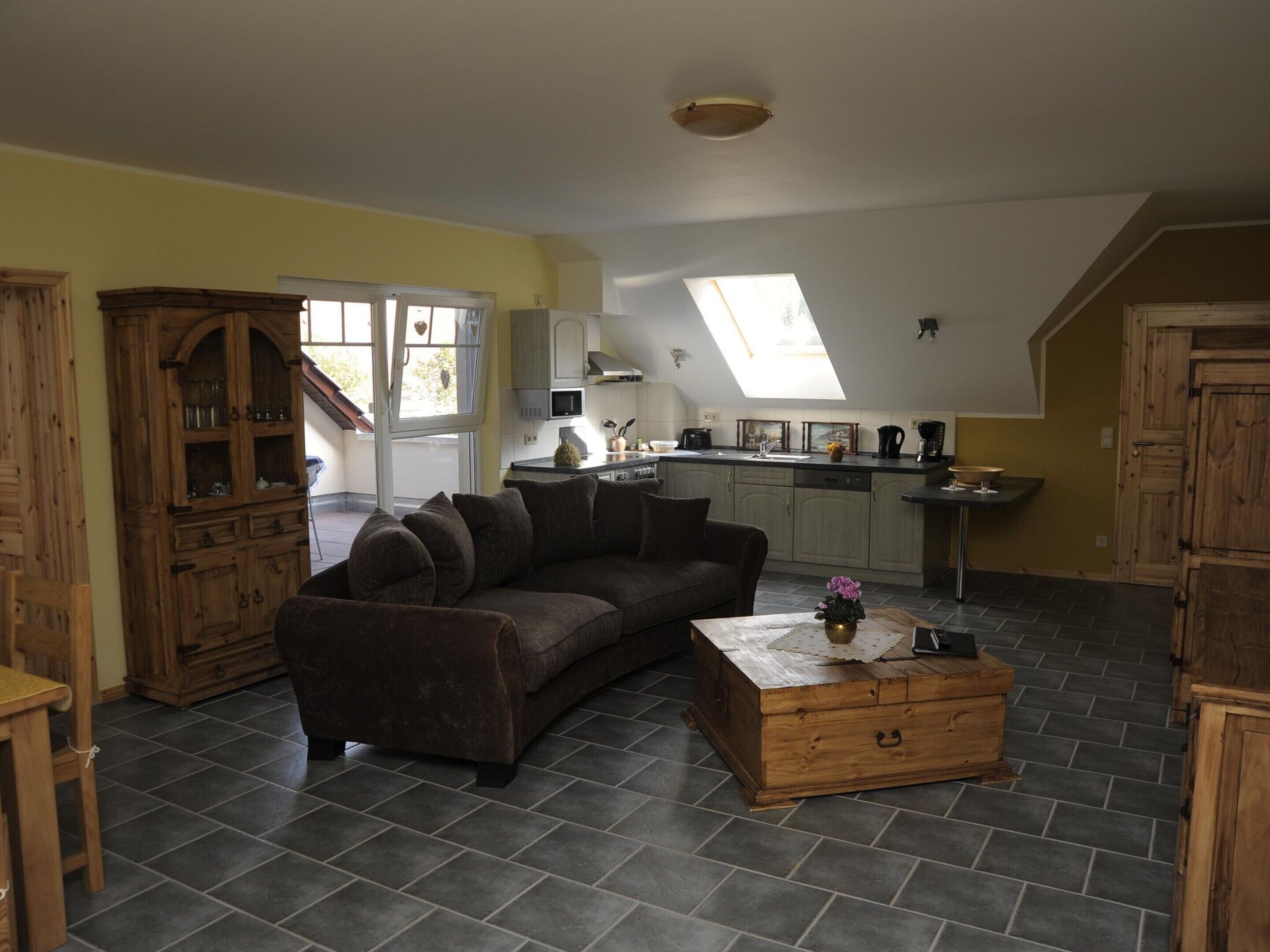Ampla sala de estar com um sofá marrom escuro, armários de madeira e piso de azulejos.