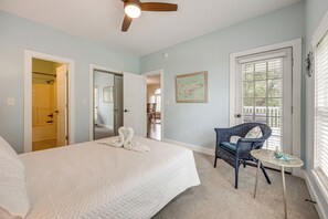 Quarto com cama, uma cadeira, uma mesinha e um ventilador de teto.