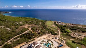 Vista aérea de um resort à beira-mar com campo de golfe, piscina e área de praia.