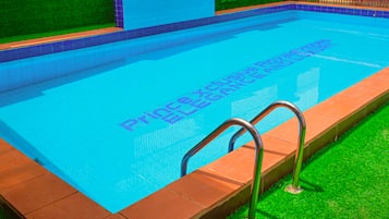 Uma piscina com interior azul, rodeada por um deck ladrilhado e um gramado verde.