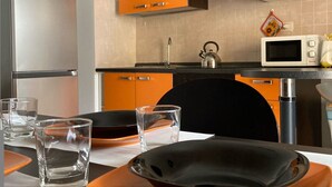 Uma cozinha moderna com armários laranja, uma geladeira de aço inoxidável, um micro-ondas e uma chaleira no balcão.
