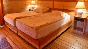 Quarto acolhedor de cabana de madeira, com duas camas, uma mesa de cabeceira com luminárias e uma cabeceira de madeira.