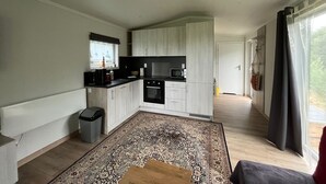 Cozinha compacta com armários brancos, micro-ondas e fogão. Há um cesto de lixo e um tapete estampado no chão.