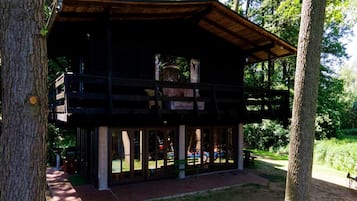 Uma cabana de madeira com varanda, rodeada por árvores e um espaço com grama.